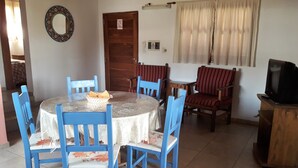 Uma sala de jantar com uma mesa redonda, cadeiras azuis e uma televisão sobre um suporte de madeira.