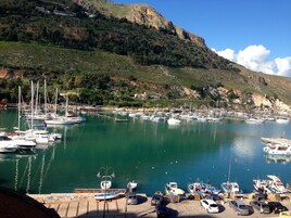 Uma marina com barcos atracados, um cais com carros e uma paisagem montanhosa ao fundo.