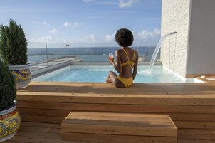 Uma pessoa sentada à beira da piscina, com vista para o mar.