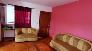 Uma sala de estar com dois sofás, uma mesa de centro de madeira, uma porta de madeira e uma janela com cortina vermelha.
