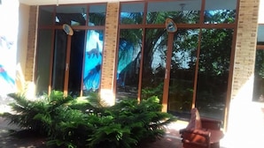 Entrada de um edifício com grandes portas de vidro, parede de tijolos e um pequeno jardim com plantas.