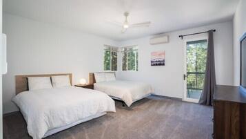 Quarto com duas camas, um ventilador de teto, janela com vista para árvores e porta com vista para vegetação.