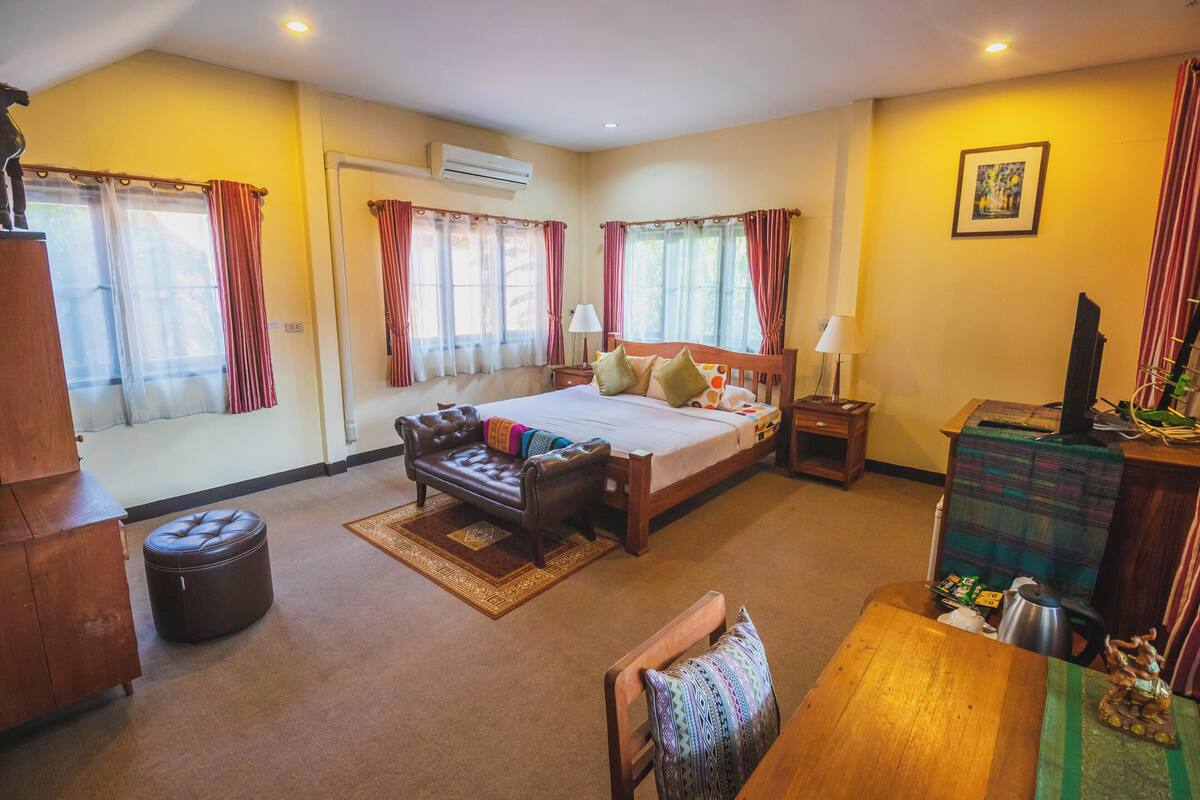 Quarto de hotel com uma cama, uma secretária de madeira, uma cadeira, um pequeno banquinho e um guarda-roupa.