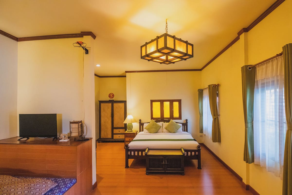 Quarto de hotel com cama, mesas de cabeceira, televisão, escrivaninha e janela com cortinas.