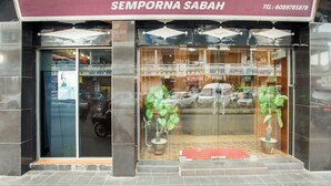 Entrada de um hotel com uma placa vinho escuro com a inscrição "GRAND INN SEMPORE SABAH" e um número de contato.