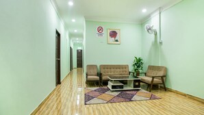 Uma área de recepção com sofá, cadeiras, mesa de centro, tapete estampado, ventoinha na parede e placa de proibido fumar.