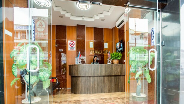 Uma área de recepção de hotel com um balcão de madeira, um tapete vermelho e portas de vidro.