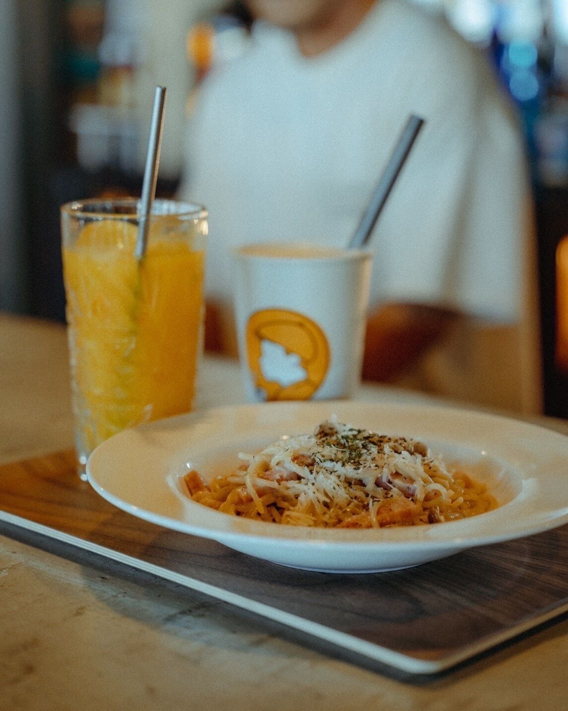 Um prato de massa acompanhado de suco de laranja e um copo com canudo.
