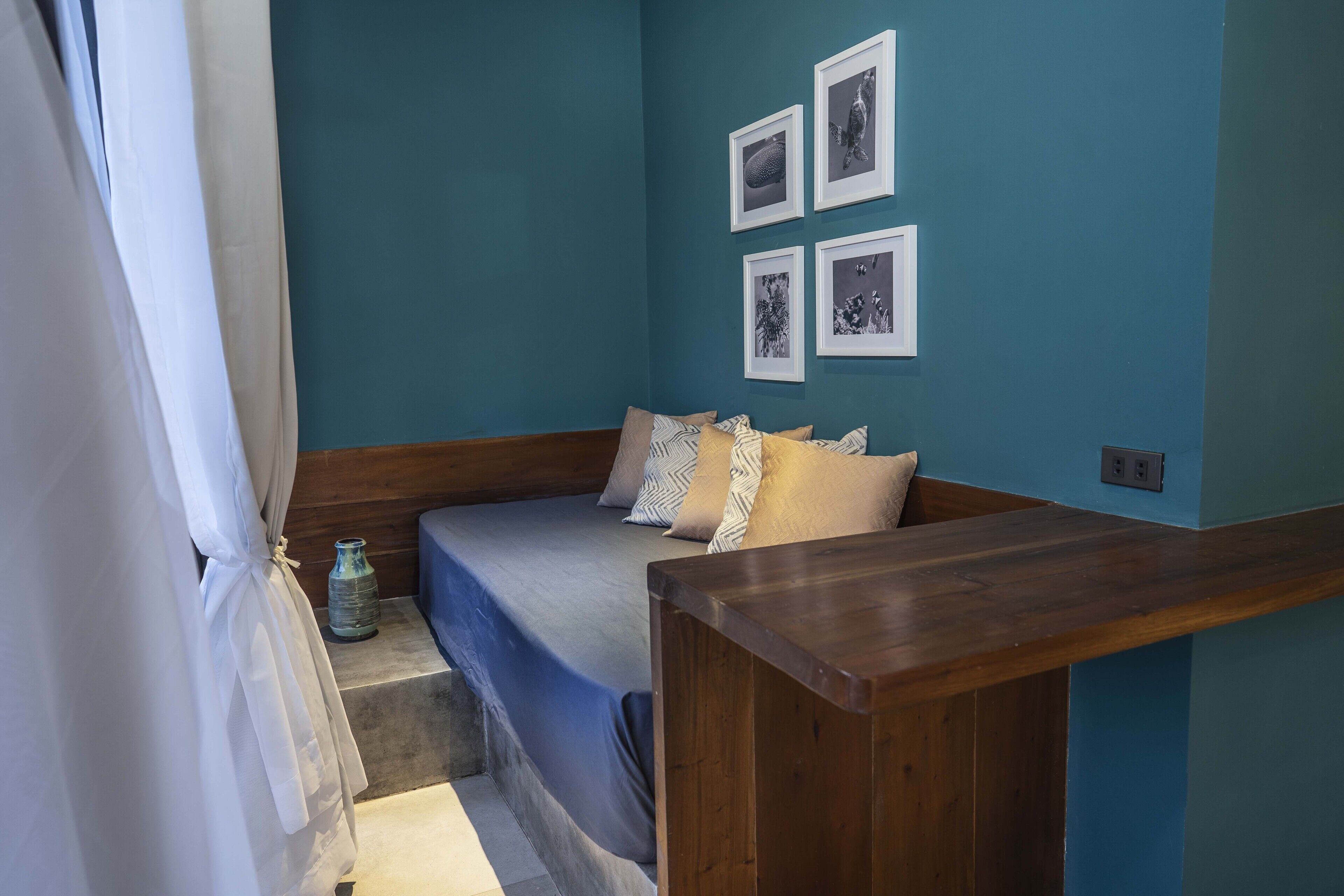 Quarto com uma cama, um banco de madeira e uma parede com quadros.