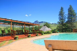 Área de piscina com pergolado de madeira, espreguiçadeiras verdes e vista para as montanhas.