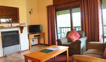 Uma sala de estar com televisão sobre um suporte de madeira, um sofá, uma mesa de centro e uma lareira.