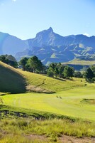 Um campo de golfe com colinas ondulantes e uma cordilheira ao fundo.
