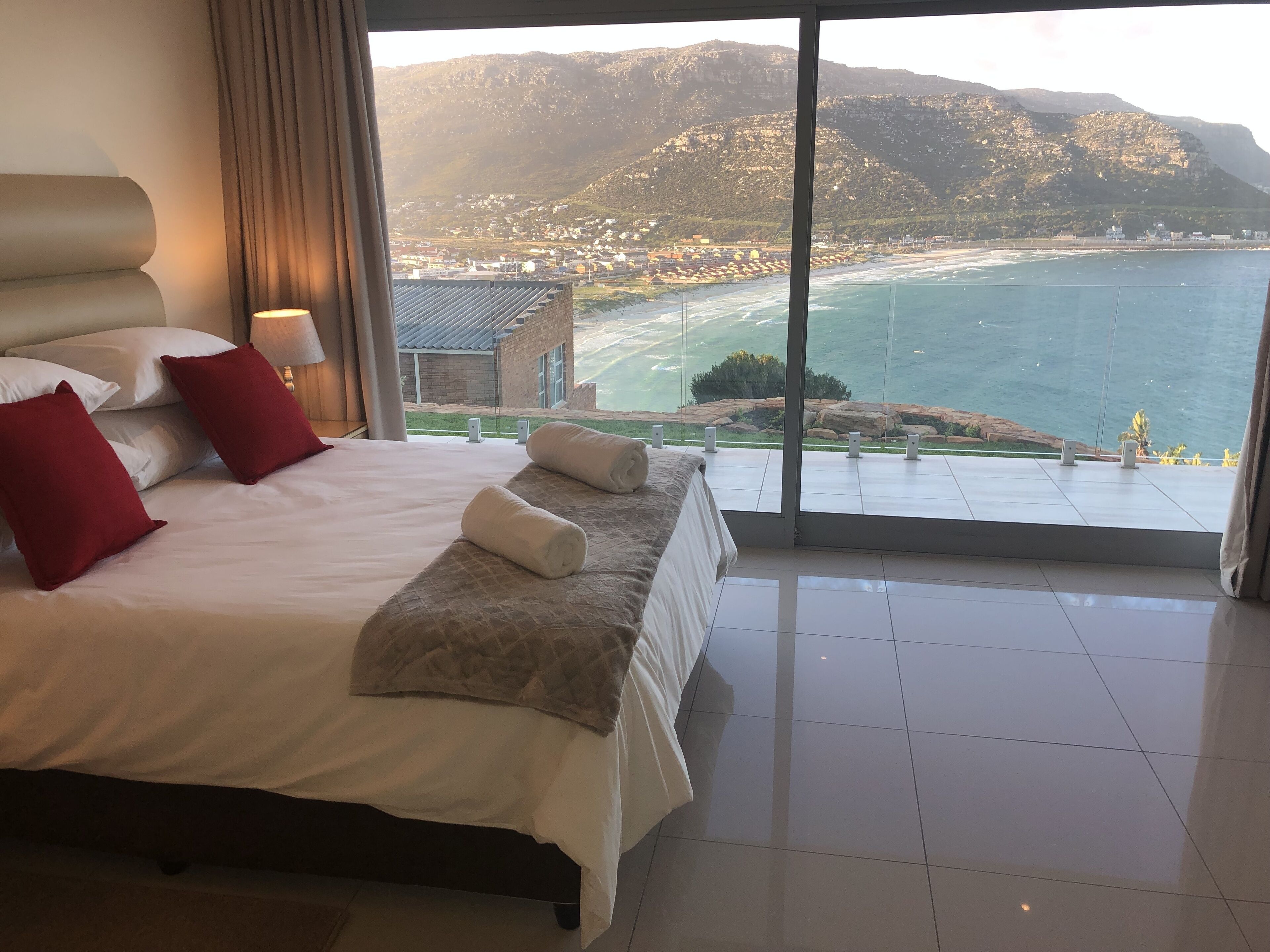 Quarto de hotel com uma cama grande, vista para o mar e uma montanha ao fundo.