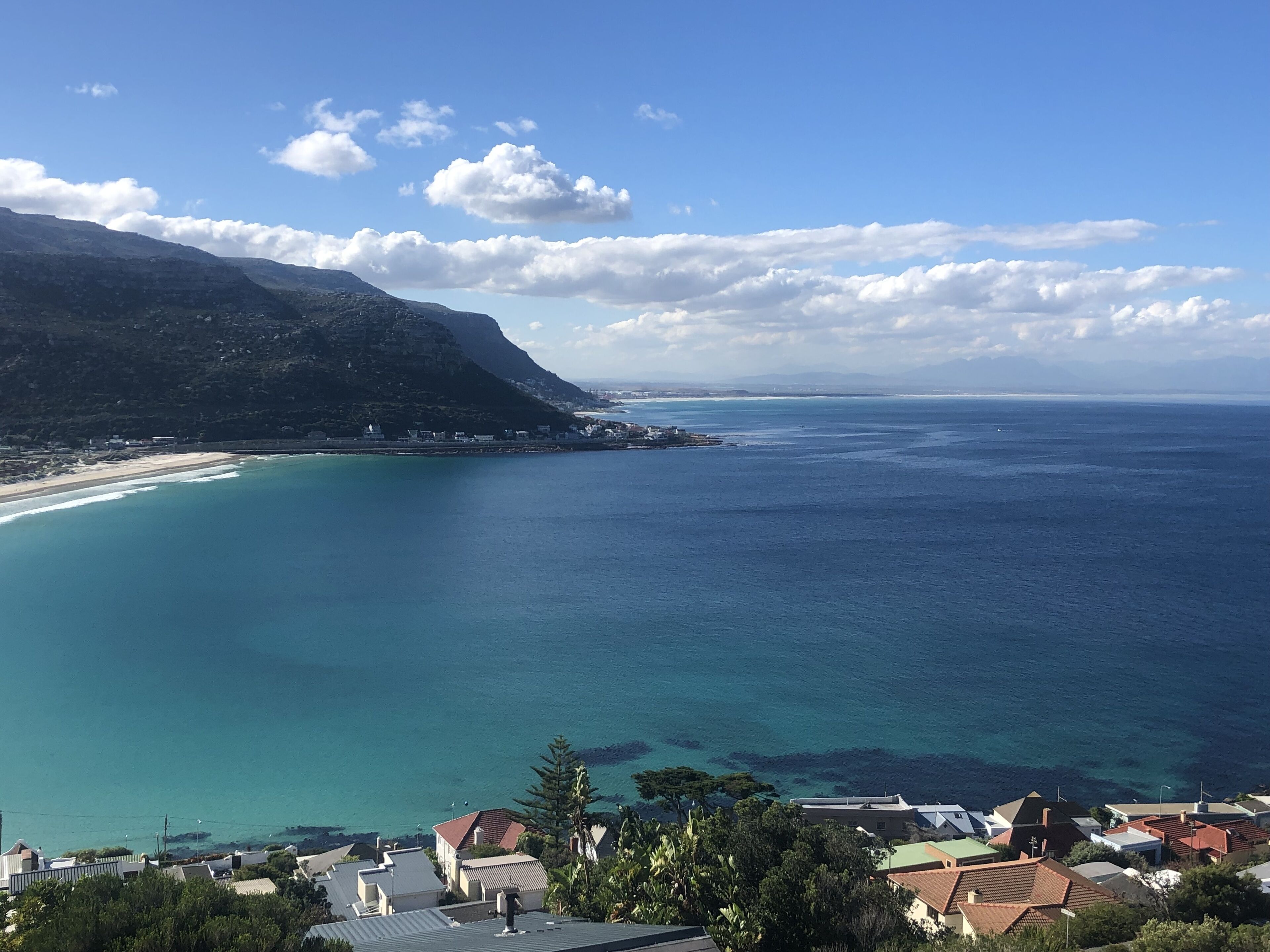 Uma vila costeira com uma praia, casas e uma montanha ao fundo.
