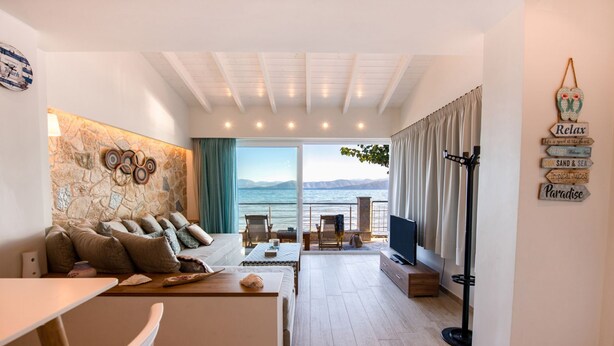 Sala de estar com sofá, televisão e vista para o mar.
