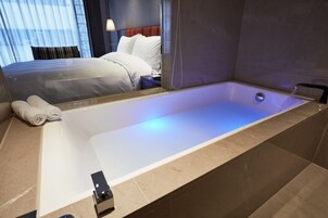 Casa de banho moderna com uma banheira grande, um espelho e uma cama com roupa de cama branca.