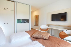 Quarto de hotel moderno com cama, televisão, escrivaninha e cadeira.