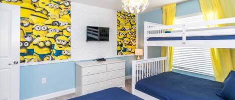 Um quarto com beliches, cômoda, penteadeira e papel de parede com tema Minion.