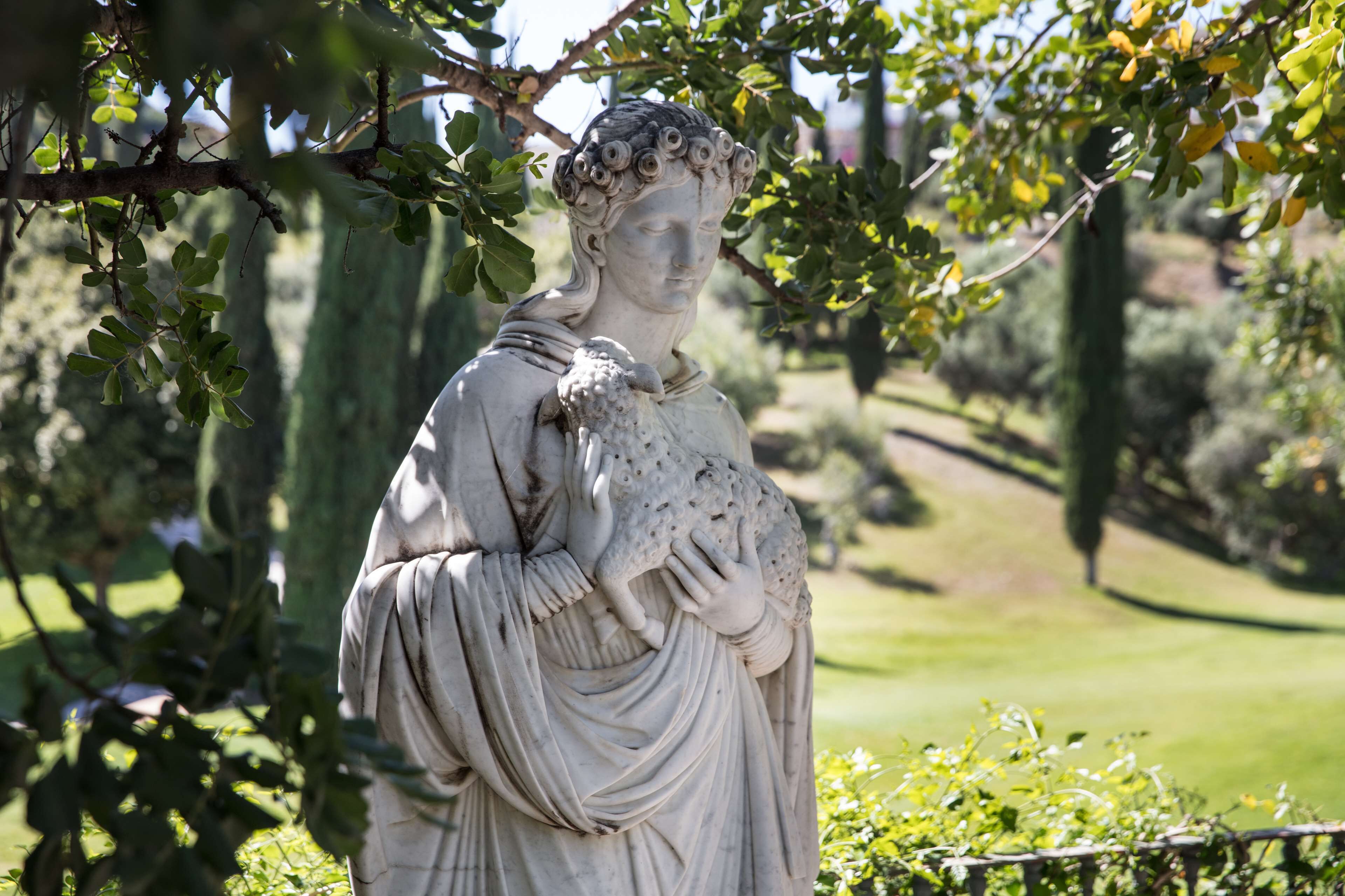 Estátua de uma mulher segurando um cordeiro em um jardim.