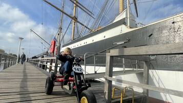 Um cais de madeira com uma pessoa andando de triciclo perto de um navio grande com mastros altos.