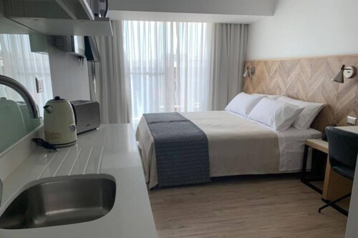 Quarto de hotel com cama, secretária, pia e janela com cortinas.