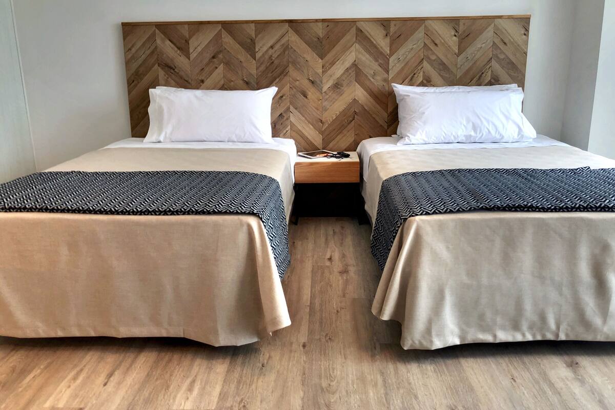 Uma cama de casal com cabeceira de madeira em padrão herringbone, duas mesas de cabeceira e um cobertor estampado.