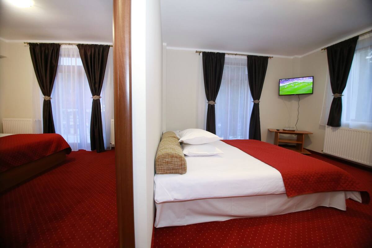 Quarto de hotel com duas camas, televisão e janela com cortinas.