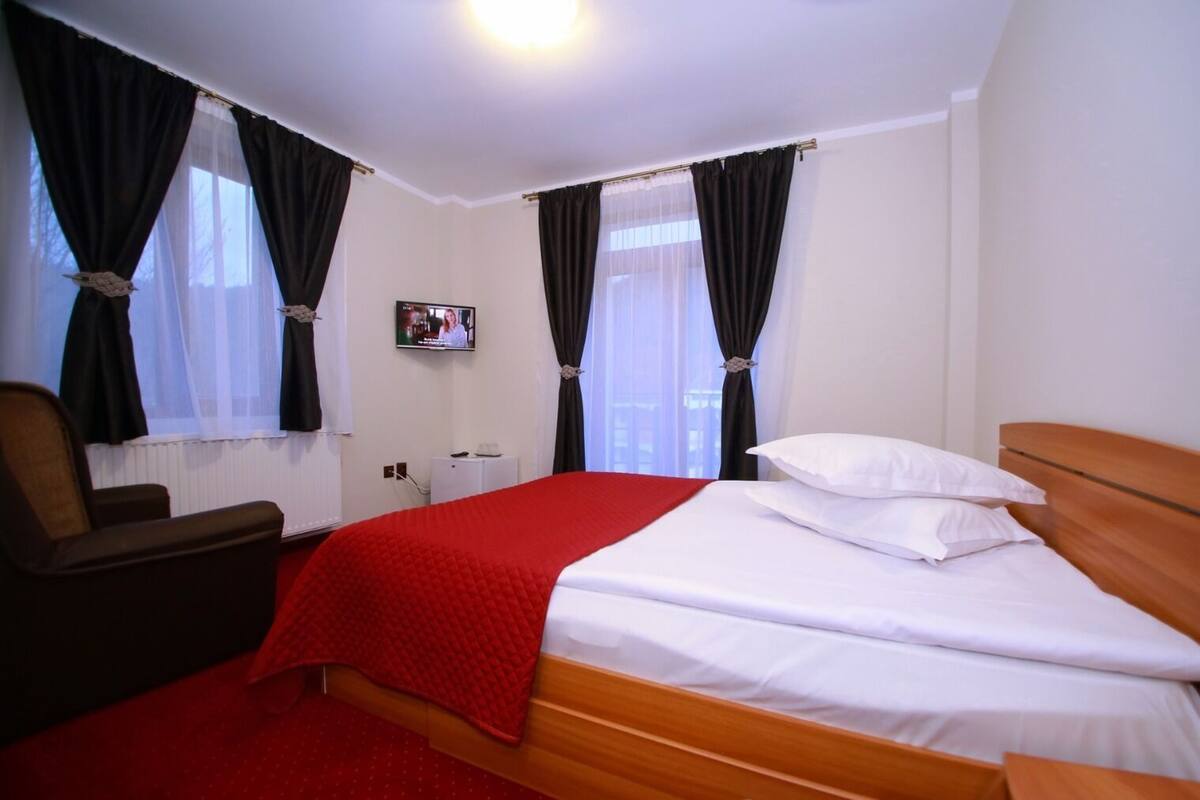 Quarto de hotel com uma cama, uma cadeira, uma televisão e uma janela com cortinas.