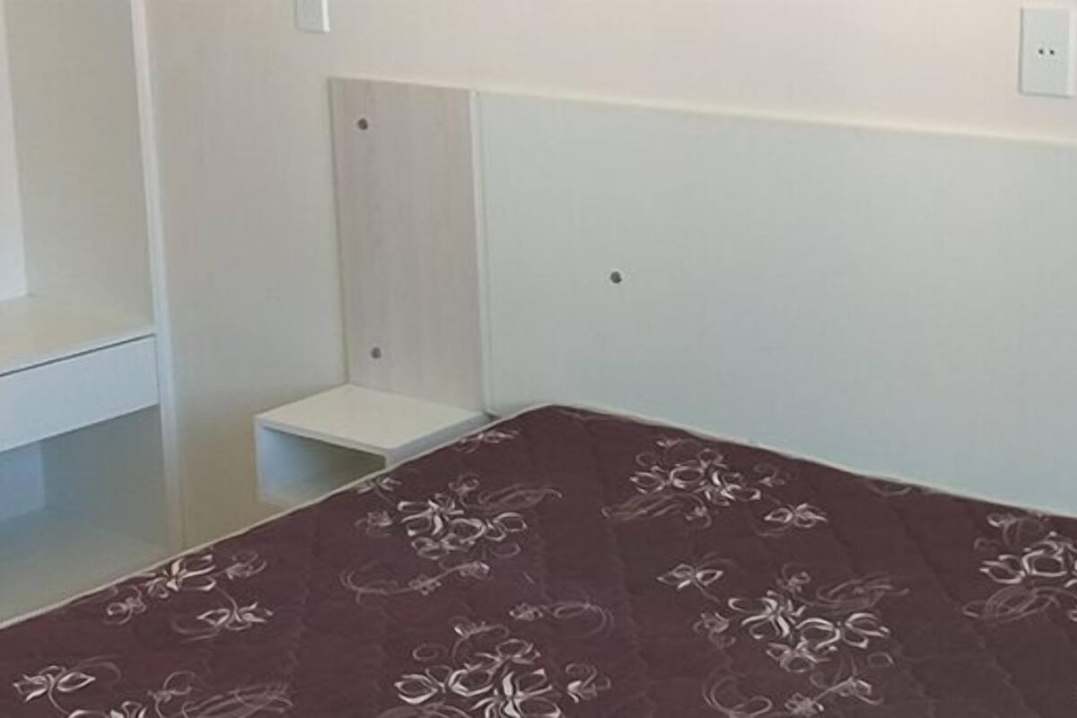 Um quarto com uma cama, um guarda-roupa branco e uma pequena mesa.