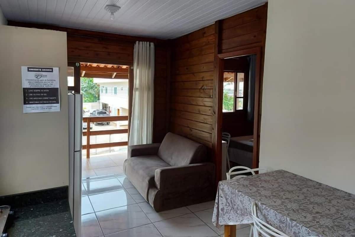 Quarto com decoração em madeira, um sofá, uma mesa de jantar e vista para o exterior.