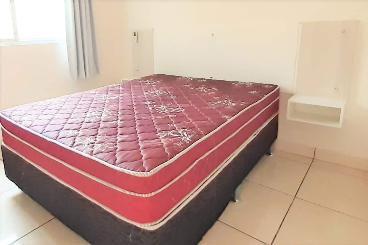 Quarto com uma cama grande, uma mesinha de cabeceira e uma prateleira na parede.