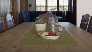 Uma mesa de jantar de madeira com um jogo de sousa verde, um prato branco com bolachas e tomates cereja, uma planta em vaso e copos decorativos.