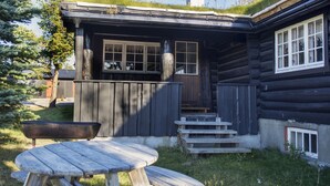 Uma cabana de toras com um alpendre de madeira, um pequeno espaço de estar ao ar livre e uma chaminé.