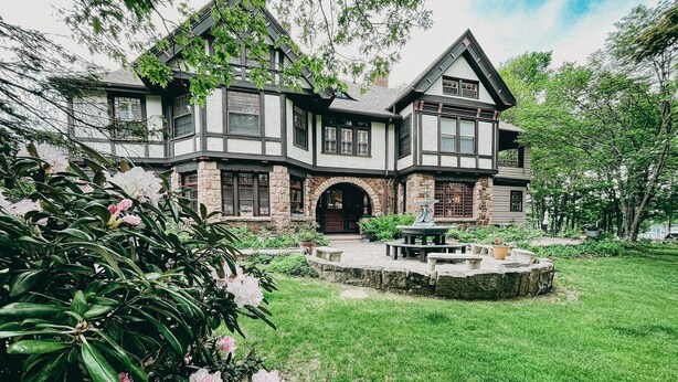 Uma casa grande de dois andares, com fundação de pedra e detalhes em madeira escura.