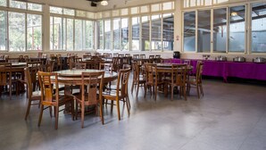 Uma ampla área de refeições interna com várias mesas e cadeiras de madeira, janelas grandes e ventiladores de teto.