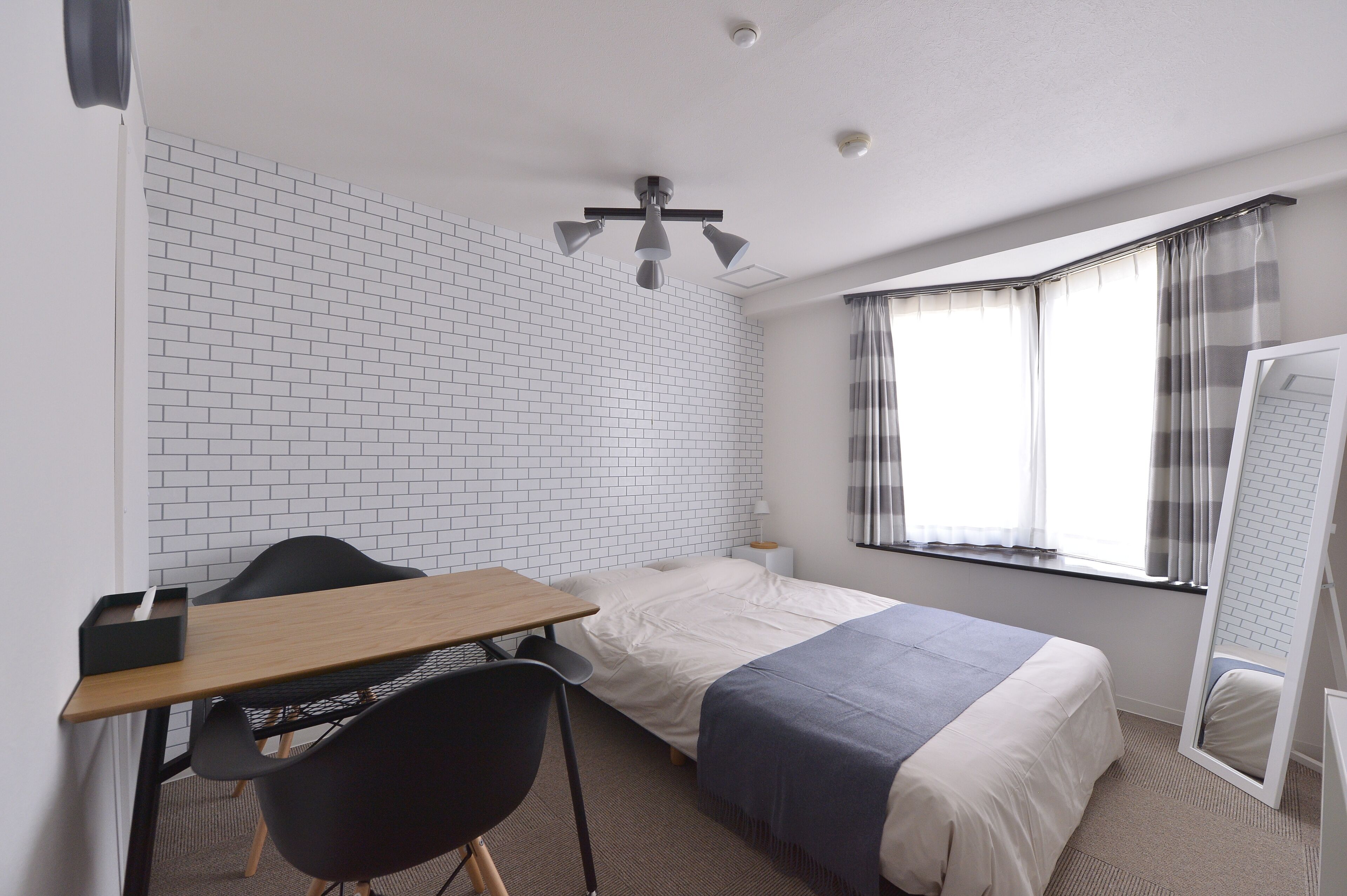 Quarto de hotel com cama, escrivaninha, cadeira, espelho e janela com cortinas.