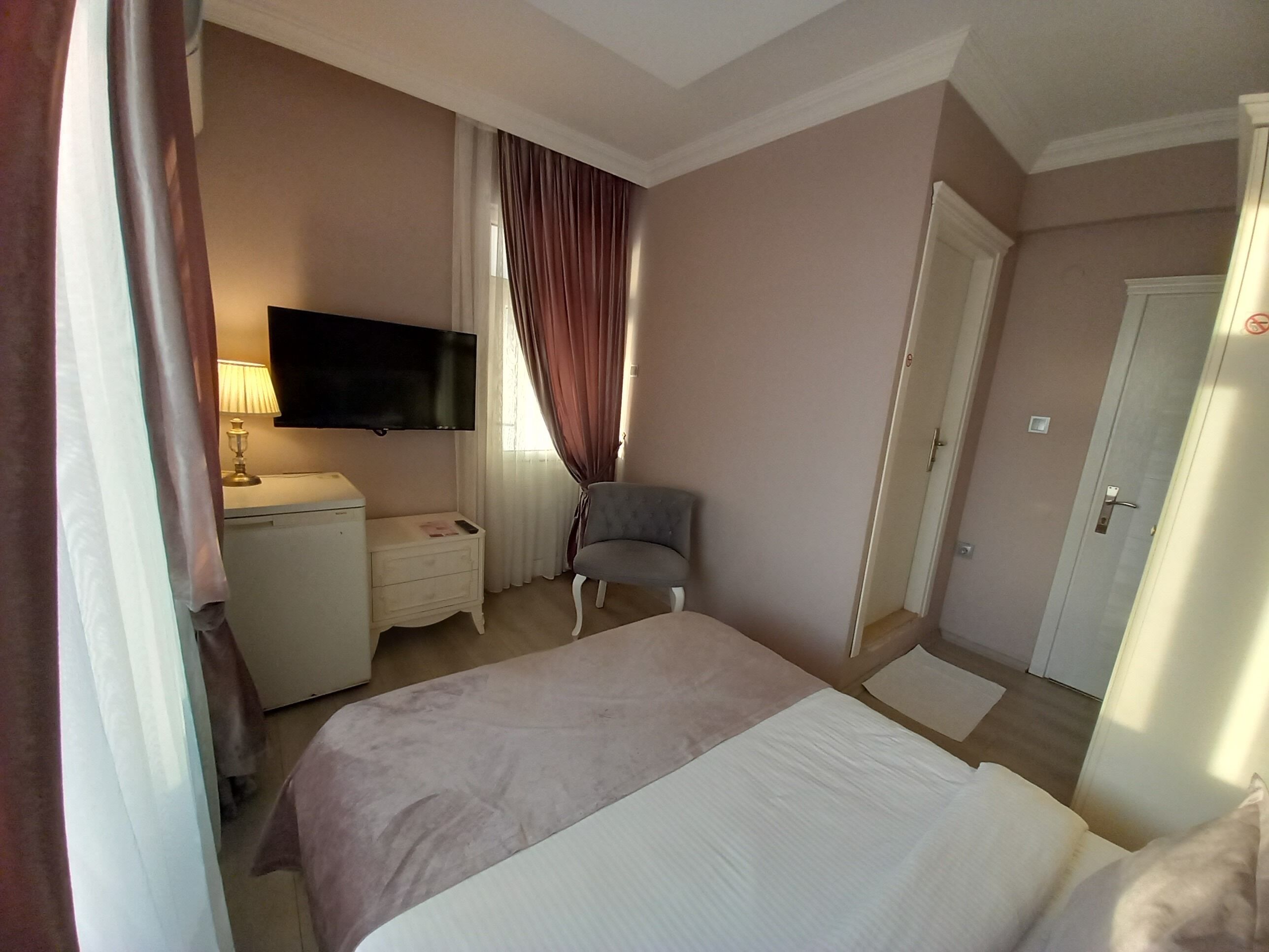 Quarto de hotel com cama, escrivaninha, cadeira, televisão e porta.