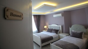 Quarto de hotel com duas camas, uma mesa de cabeceira com abajur, um aparelho de ar condicionado e um aviso na parede.