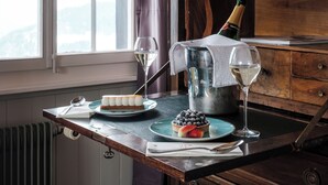 Uma mesa de madeira com uma garrafa de champanhe, duas taças de vinho, um prato com sobremesa e um livro sobre a mesa.