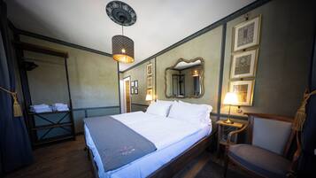 Quarto de hotel com uma cama grande, uma cadeira, uma escrivaninha com abajur, espelho e guarda-roupa.