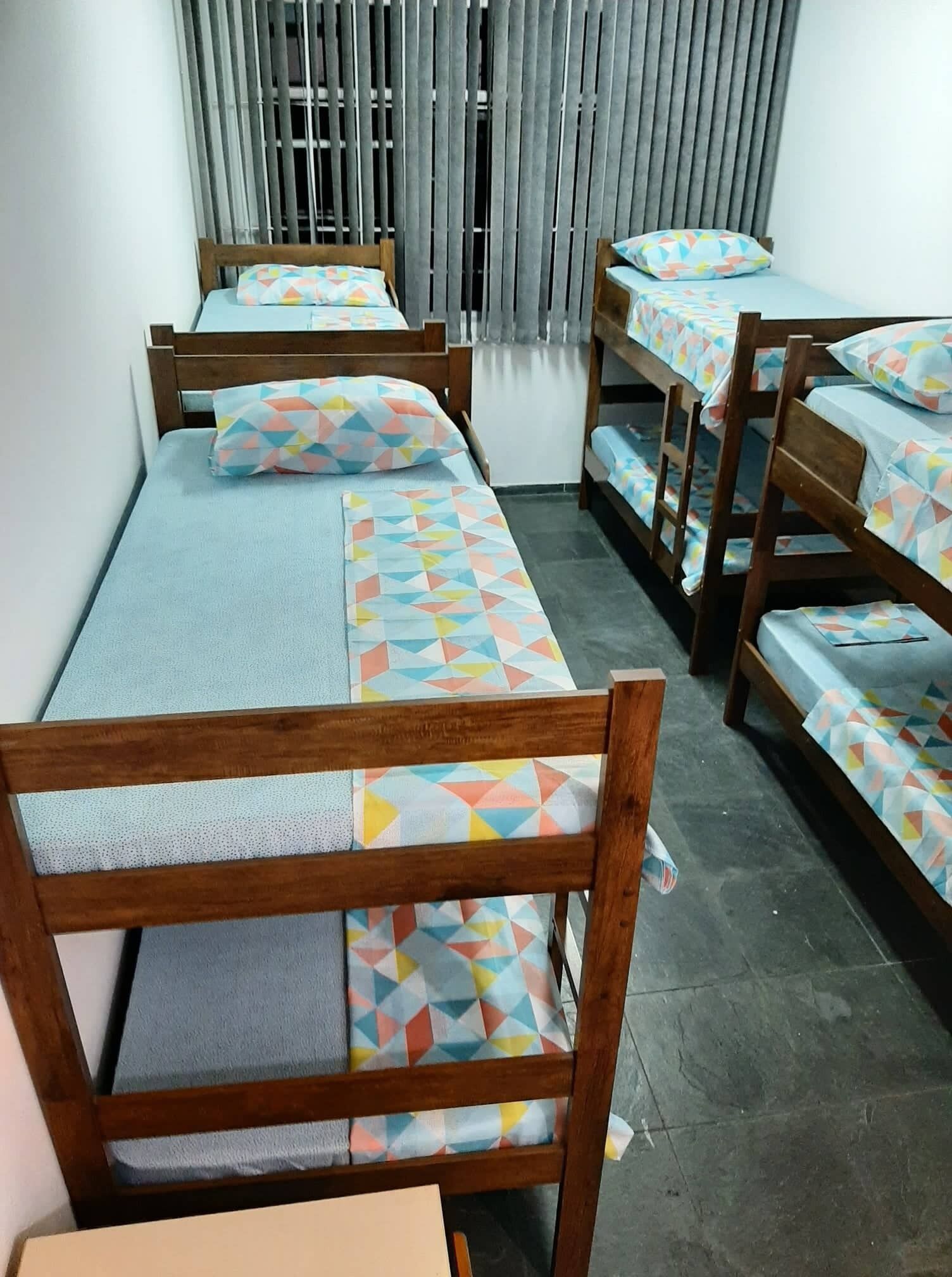 Quarto de dormitório com beliches e janela com venezianas verticais.