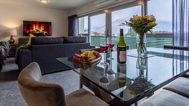 Uma sala de estar moderna com mesa de vidro, sofá, televisão e vista panorâmica através de grandes janelas.