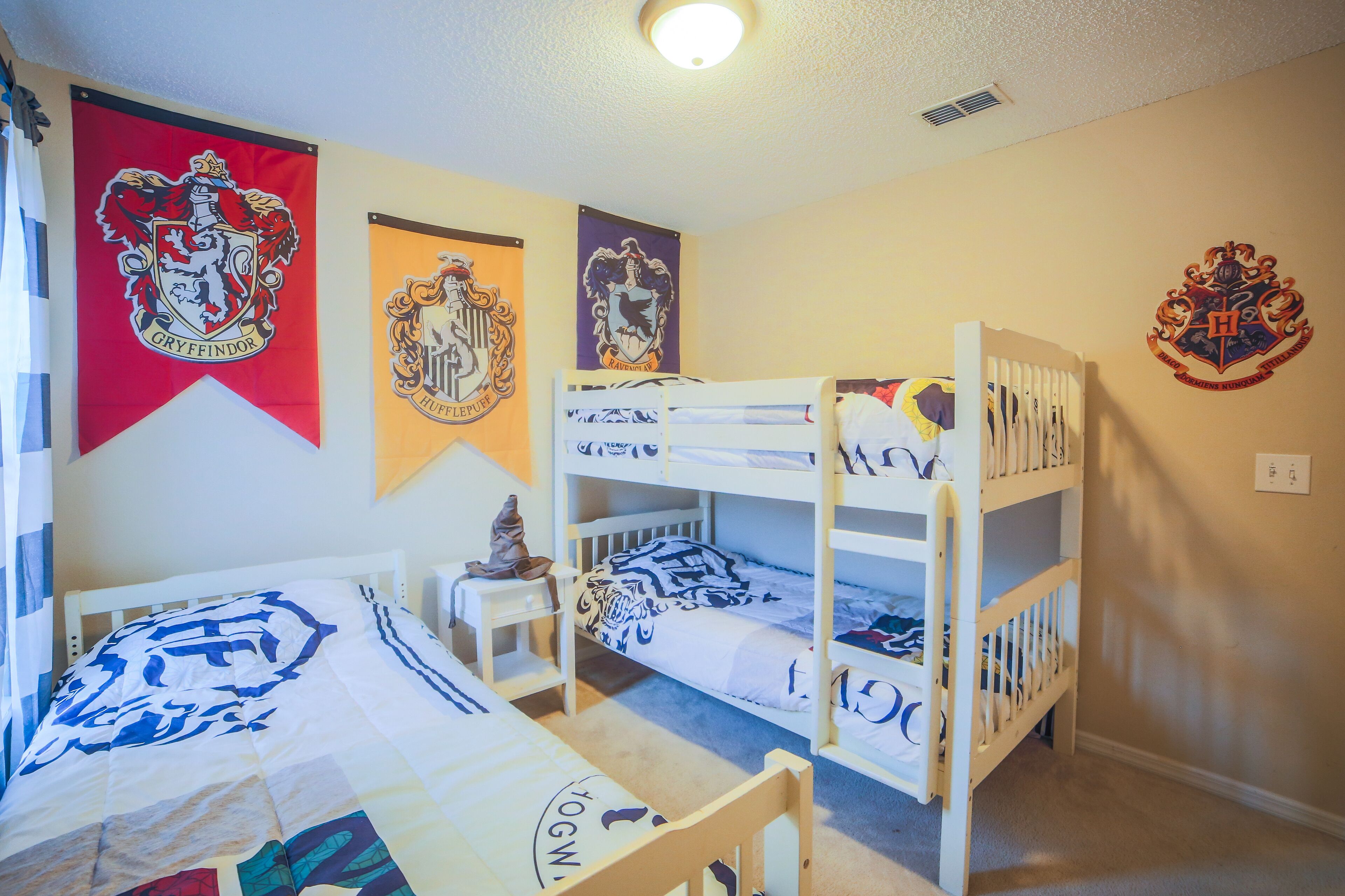 Quarto com beliches, escrivaninha e cadeira. Três faixas na parede, cada uma com um brasão diferente.