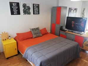Quarto com cama, televisão, guarda-roupa e mesa de cabeceira.