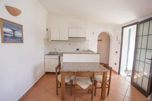 Uma cozinha compacta com armários brancos, bancada de granito e uma mesa de jantar com cadeiras.