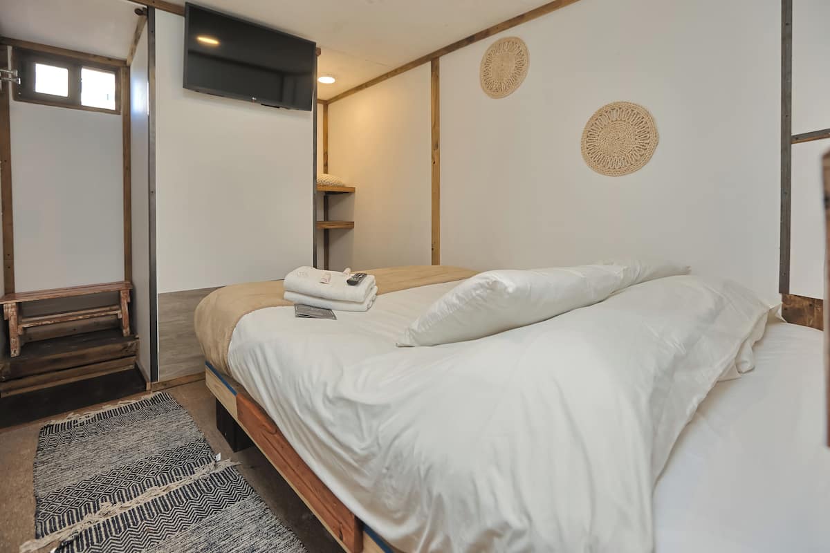 Quarto com uma cama, uma televisão fixada na parede e um banco de madeira.