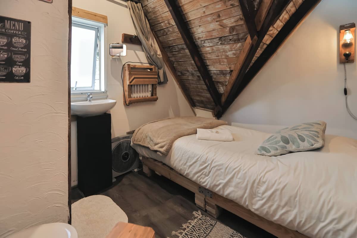Quarto com cama de madeira, janela, pia e luminária na parede.