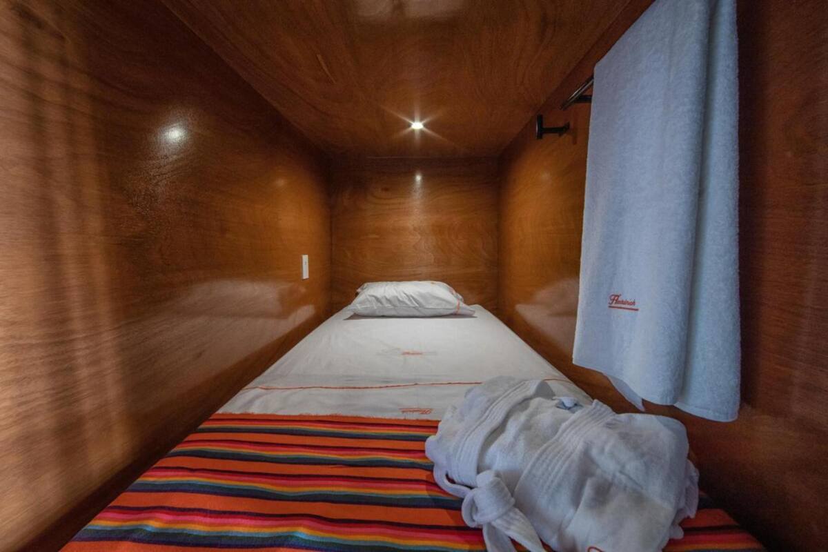 Uma cama de solteiro com manta listrada e toalha branca, paredes de madeira e uma luminária no teto.