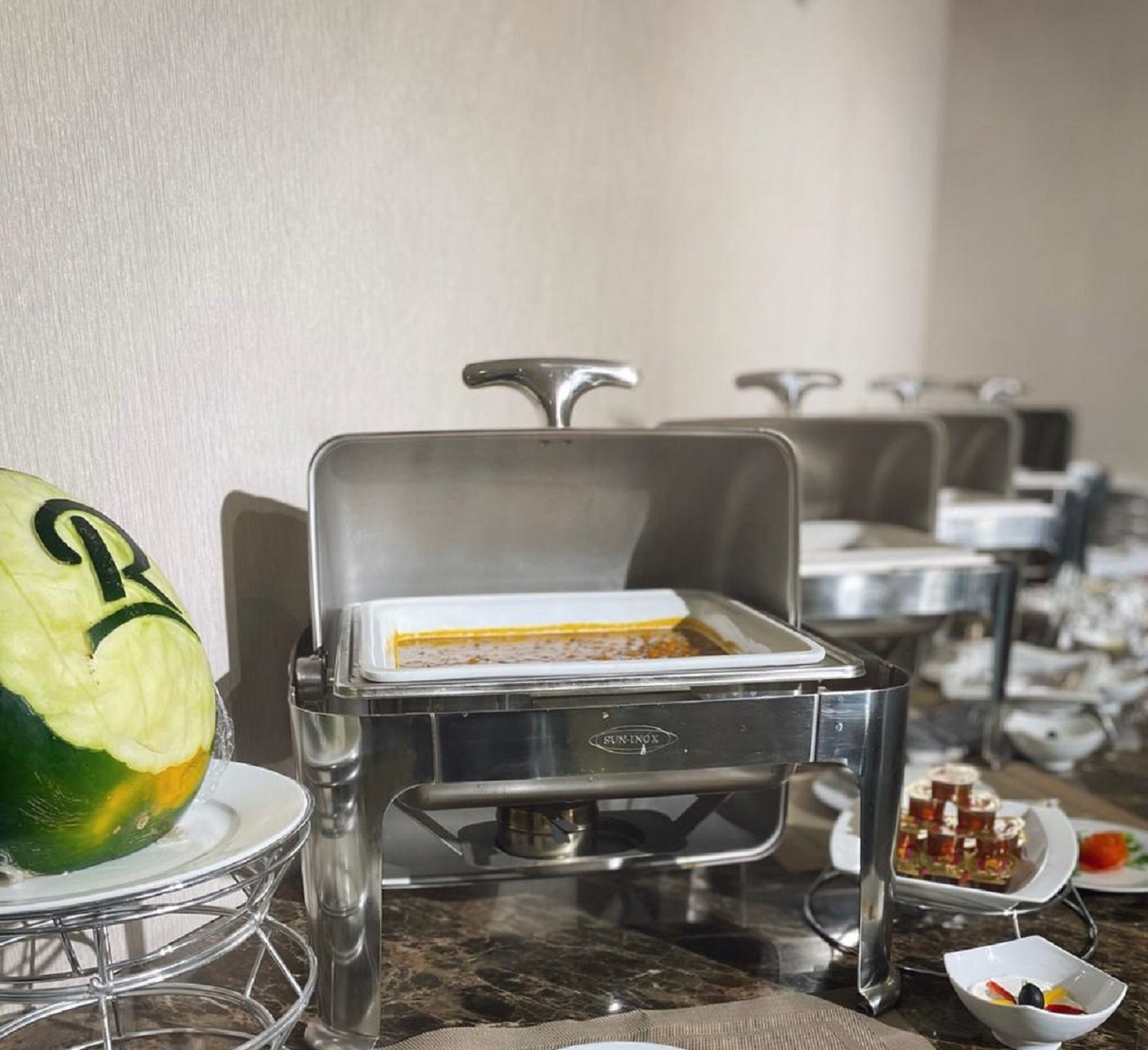 Disposição de buffet com diversos tipos de comida, incluindo uma melancia e uma bandeja de alimentos.