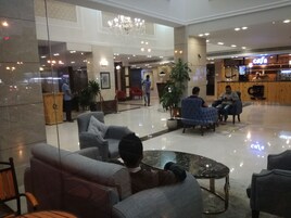 Um saguão de hotel com áreas de estar, balcão de recepção e café.